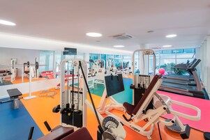 Uma academia com diversos equipamentos de exercícios, esteira e espelho.