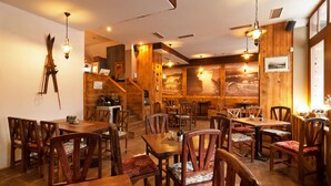 Um restaurante com interiores de madeira, várias mesas e cadeiras, e uma escadaria que leva a um andar superior.