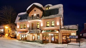 Um hotel com bar e restaurante no andar térreo, uma loja à esquerda e uma varanda com grades.