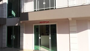 Um edifício com área de recepção, portas de vidro e varanda com corrimão branco.