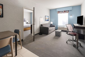 Quarto de hotel com cama, sofá, escrivaninha, cadeira, televisão e janela.