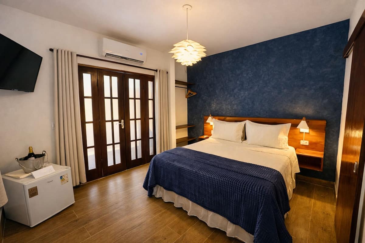 Quarto de hotel com cama, abajures, minibar, televisão e ar condicionado.