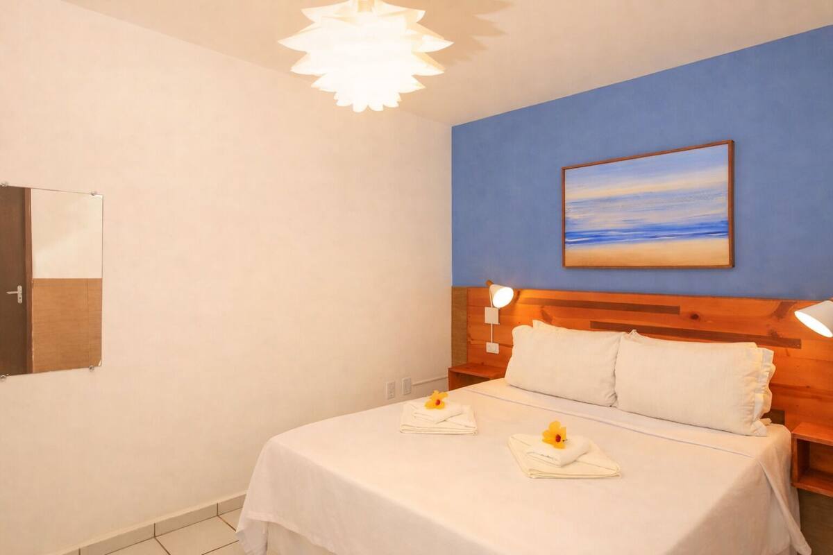 Quarto de hotel com uma cama, um quadro na parede e uma mesa de cabeceira com uma luminária.