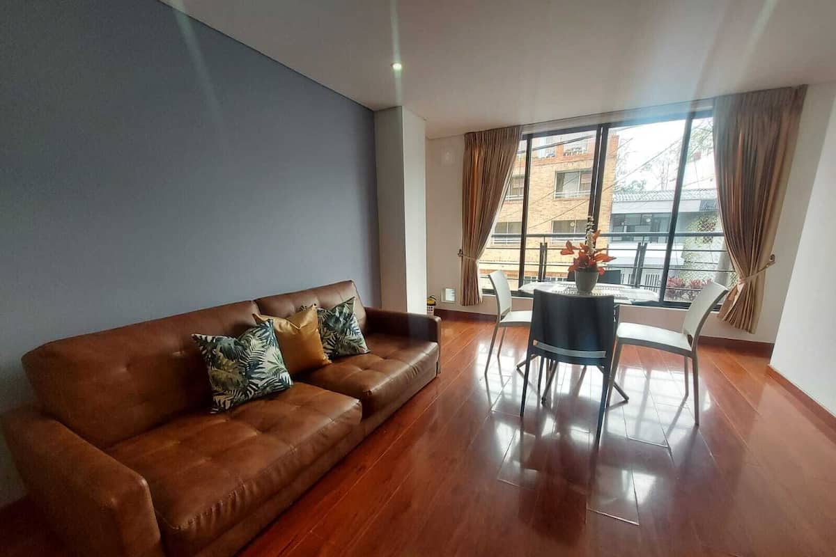 Uma sala de estar moderna com um sofá de couro marrom, uma mesa de jantar com cadeiras e janelas grandes com cortinas.