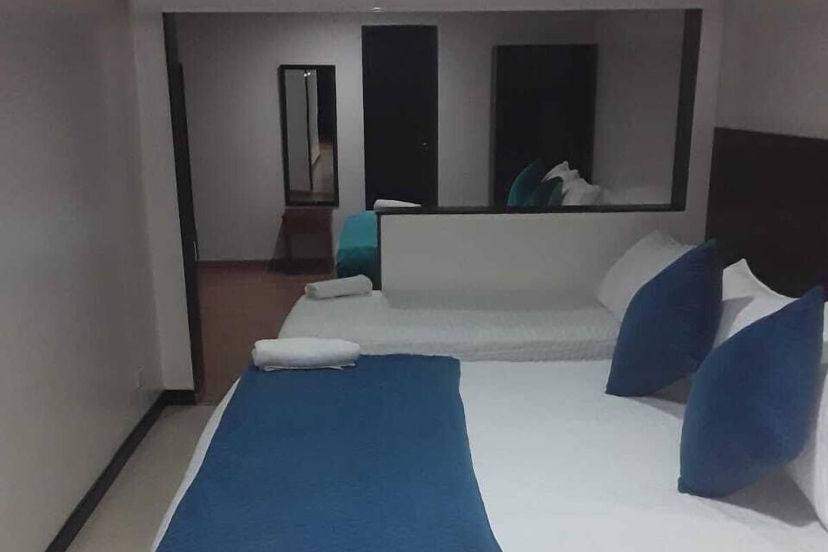 Quarto de hotel com uma cama grande, uma cama menor e um espaço de estar com uma cadeira e uma mesa.