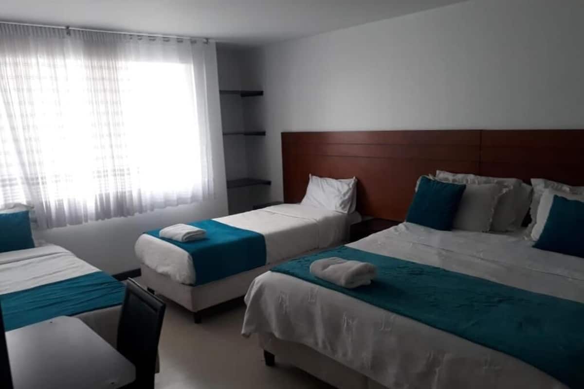 Quarto de hotel com duas camas, uma escrivaninha e uma cadeira.