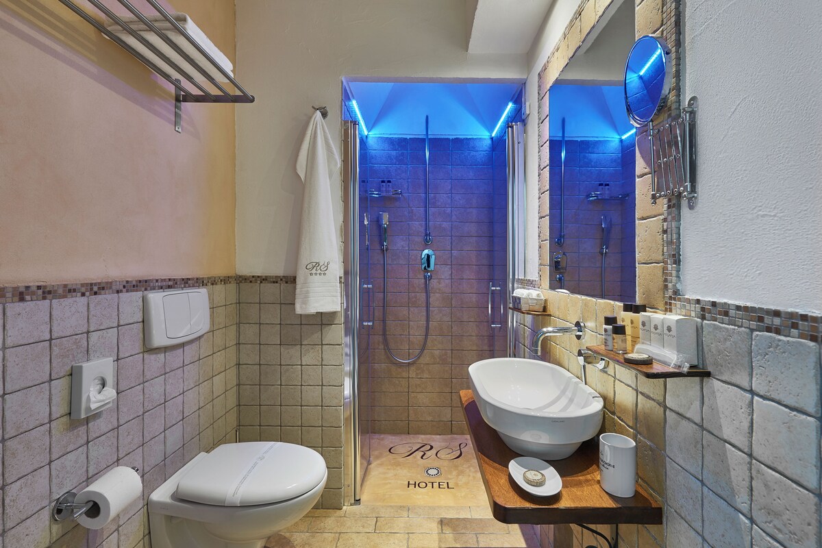 Uma casa de banho moderna com chuveiro, sanita, lavatório e um porta-toalhas.
