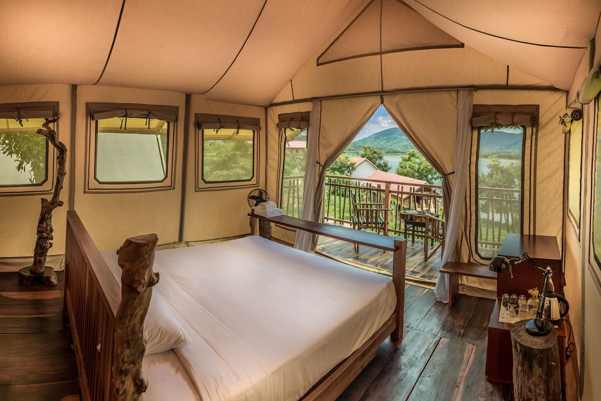 Quarto com tenda, cama, móveis de madeira e janelas amplas com vista para o exterior.