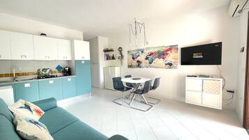 Um espaço de estar moderno com cozinha, área de refeições e TV fixada na parede.