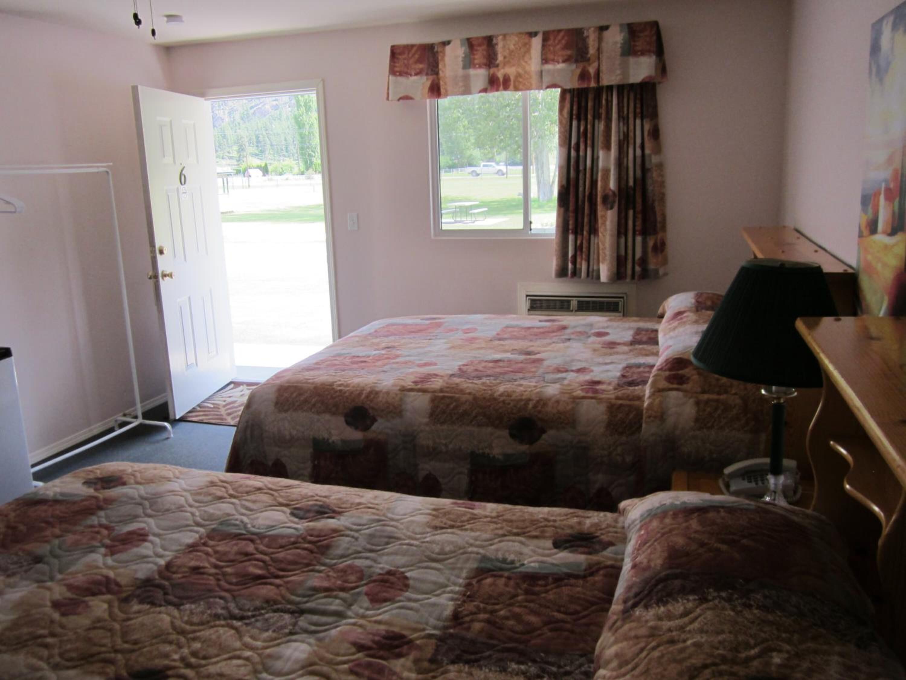 Quarto com duas camas, janela com cortinas, radiador e abajur.