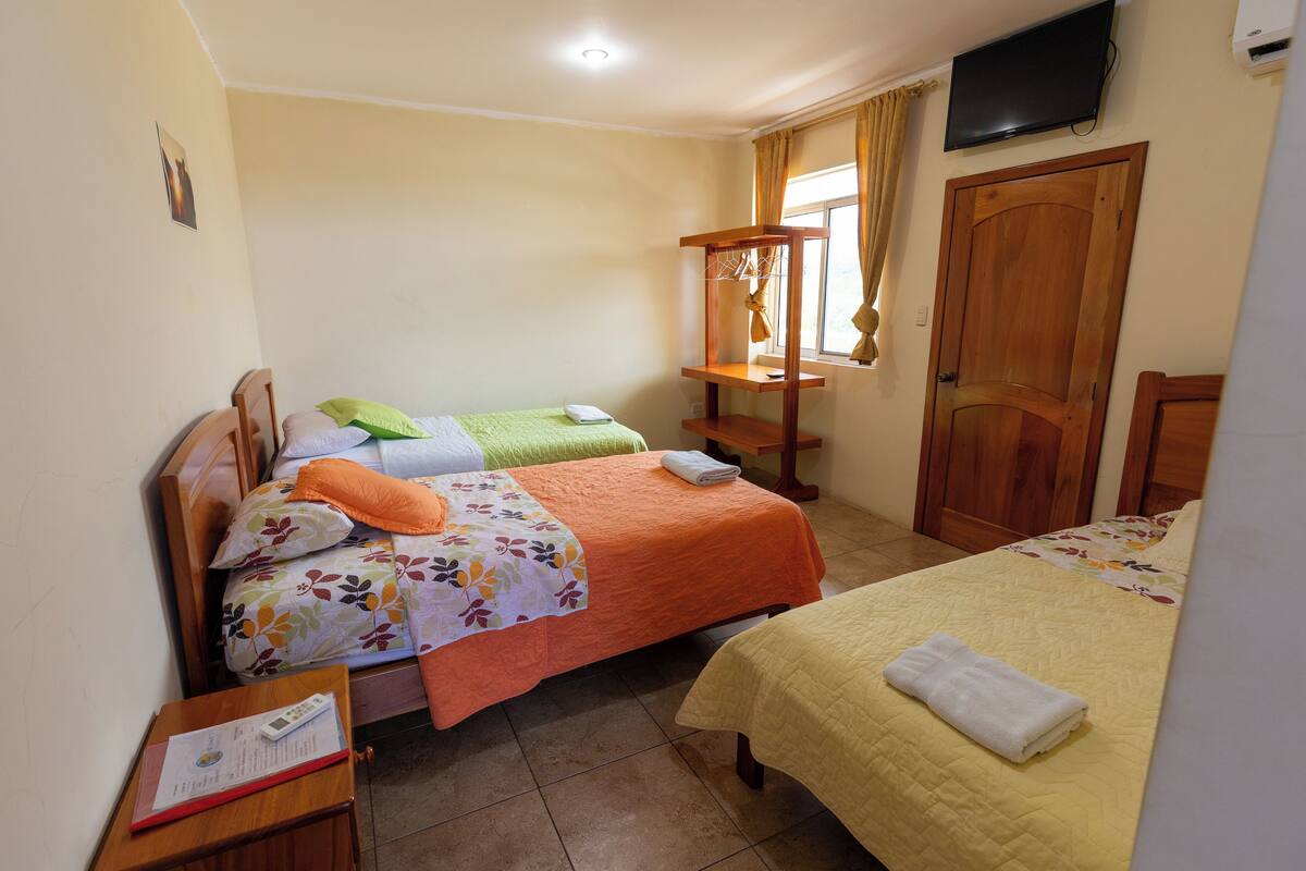 Quarto de hotel com duas camas, um guarda-roupa de madeira, uma televisão e uma janela com cortinas.