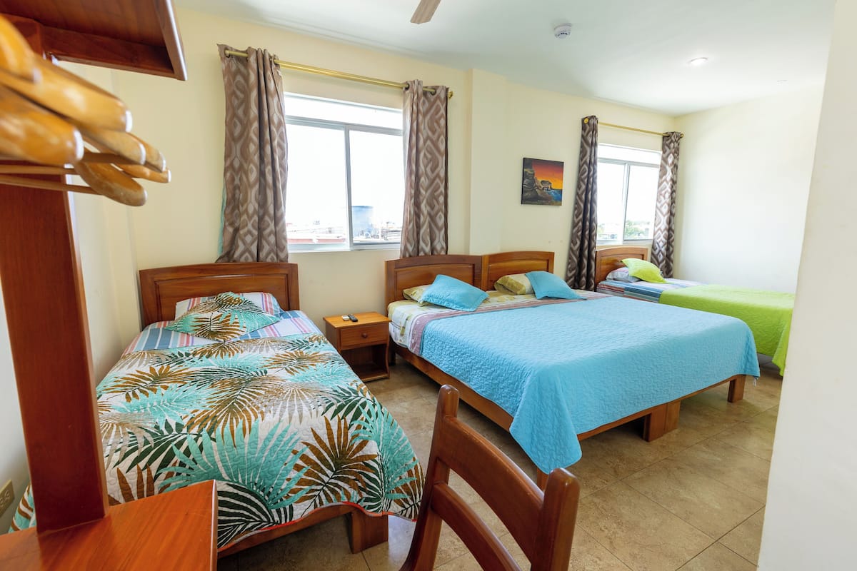 Quarto de hotel com duas camas, uma cabeceira de madeira, uma mesa de cabeceira e uma janela com cortinas.