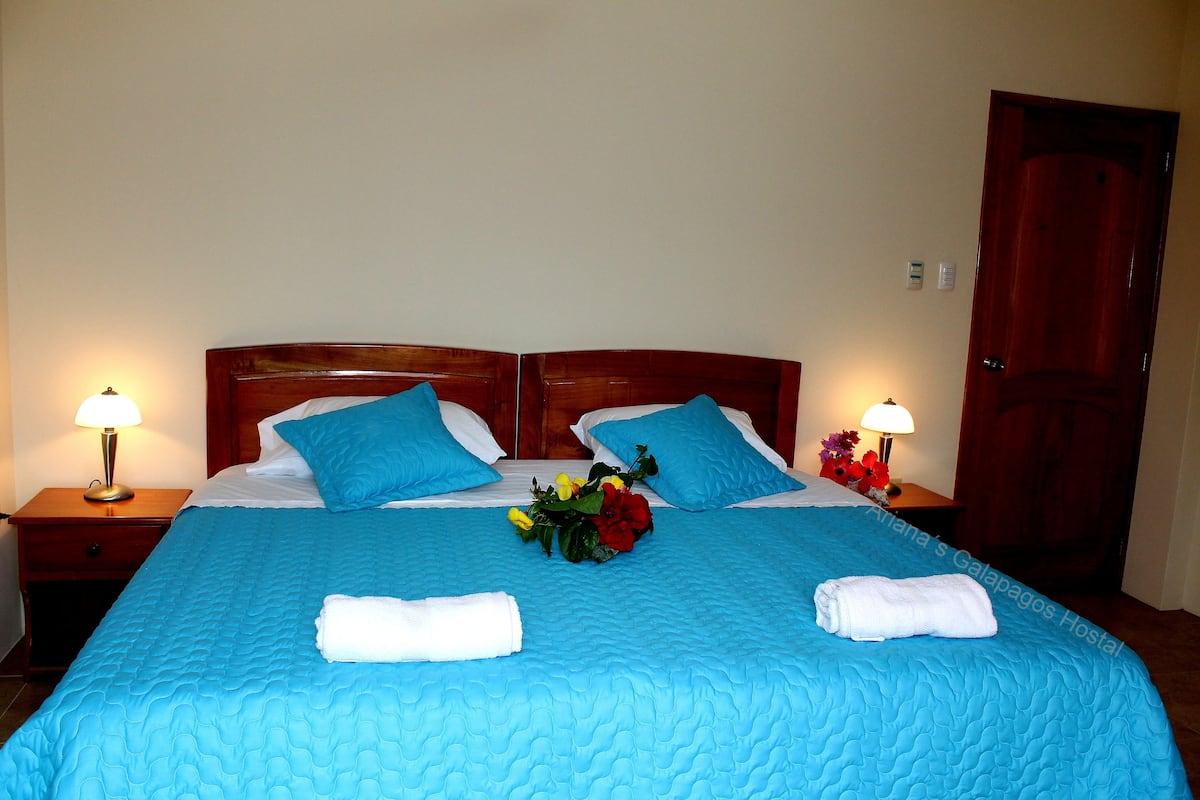 Cama bem arrumada com roupa de cama azul, dois travesseiros, um buquê de flores e duas toalhas dobradas.