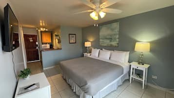 Quarto com cama grande, ventilador de teto, abajures, televisão e vista para a cozinha.
