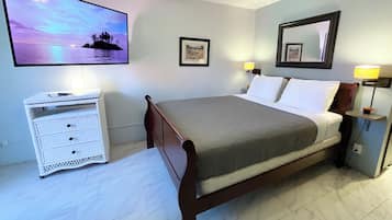 Quarto com cama, televisão na parede, cômoda e mesa de cabeceira com abajur.