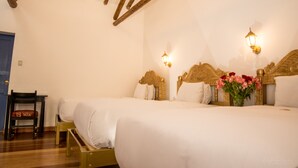 Quarto de hotel com duas camas, vigas de madeira no teto, uma cadeira e um vaso com flores.
