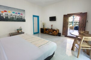 Quarto com cama, penteadeira de madeira, televisão e área de refeições com cadeiras e mesa.