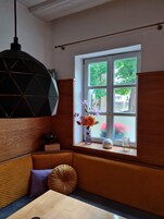 Uma área de estar aconchegante com um banco de madeira, uma mesa pequena e uma janela com vista para o verde lá fora.