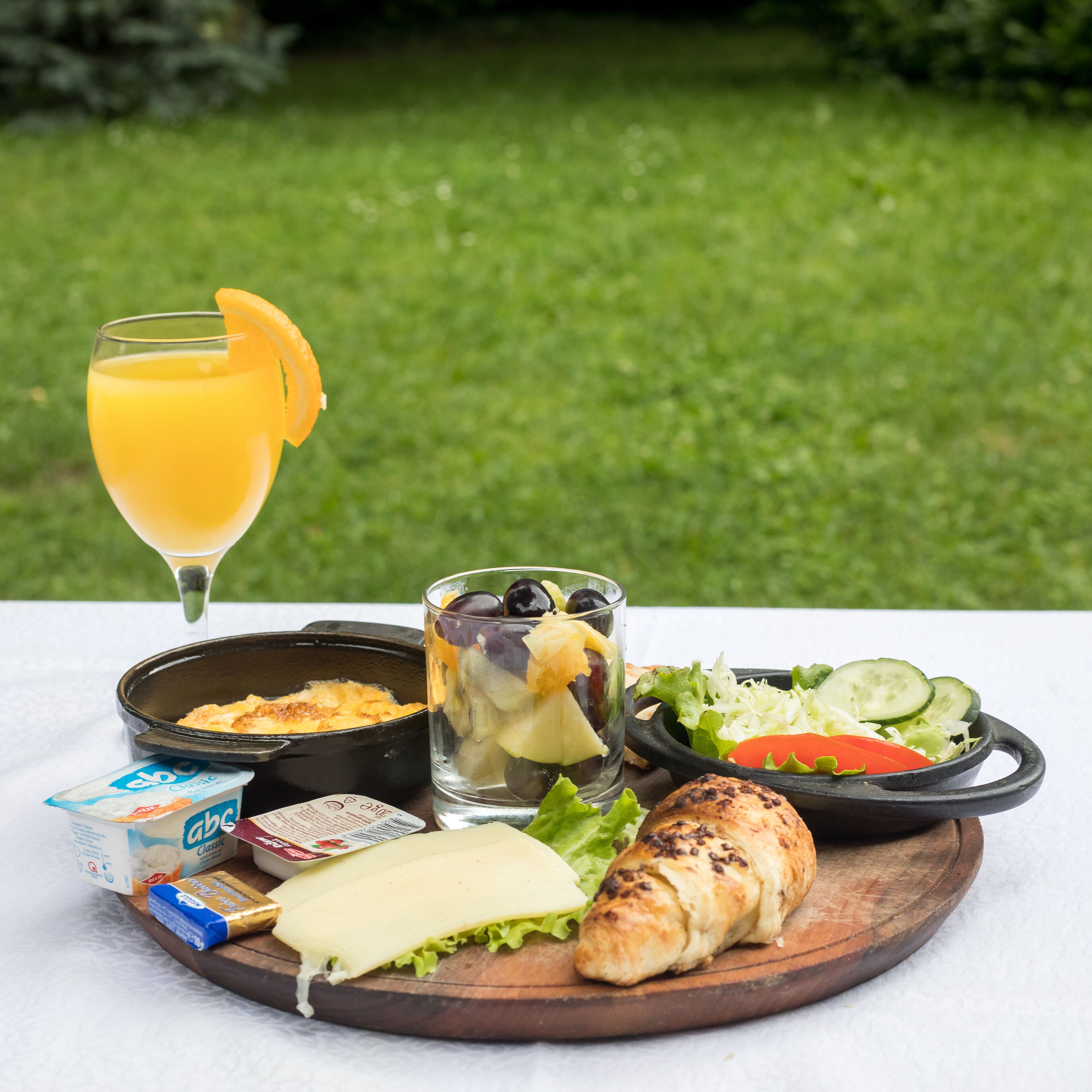 Disposição de alimentos com um croissant, queijo, salada e uma bebida sobre uma tábua de madeira.