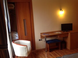 Quarto compacto com uma escrivaninha de madeira, televisão, cadeira e uma cama.