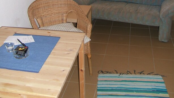 Uma sala de estar aconchegante com uma mesa de madeira, cadeiras de vime, um sofá e uma luminária.