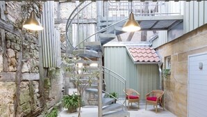 Um pátio com escadaria em espiral, plantas em vasos e duas cadeiras de vime com almofadas vermelhas.