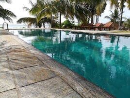 Uma piscina com água cristalina, rodeada por palmeiras e espreguiçadeiras de madeira.