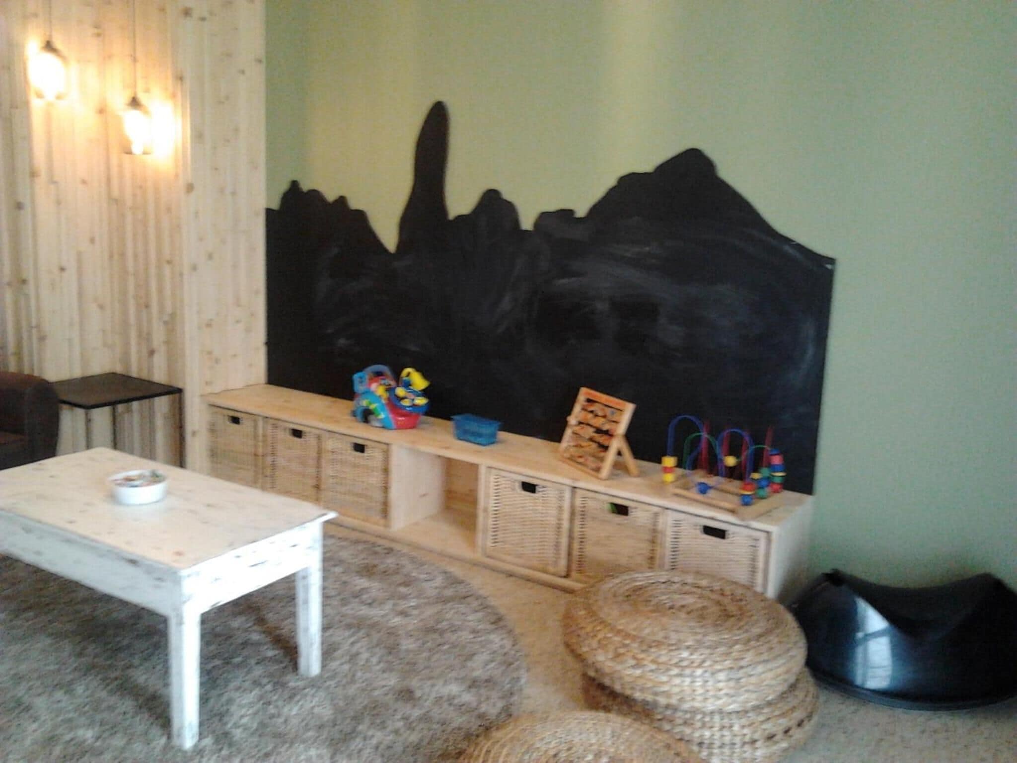 Quarto com uma mesa branca, cestos de vime, uma obra de arte preta na parede e um pufe preto.