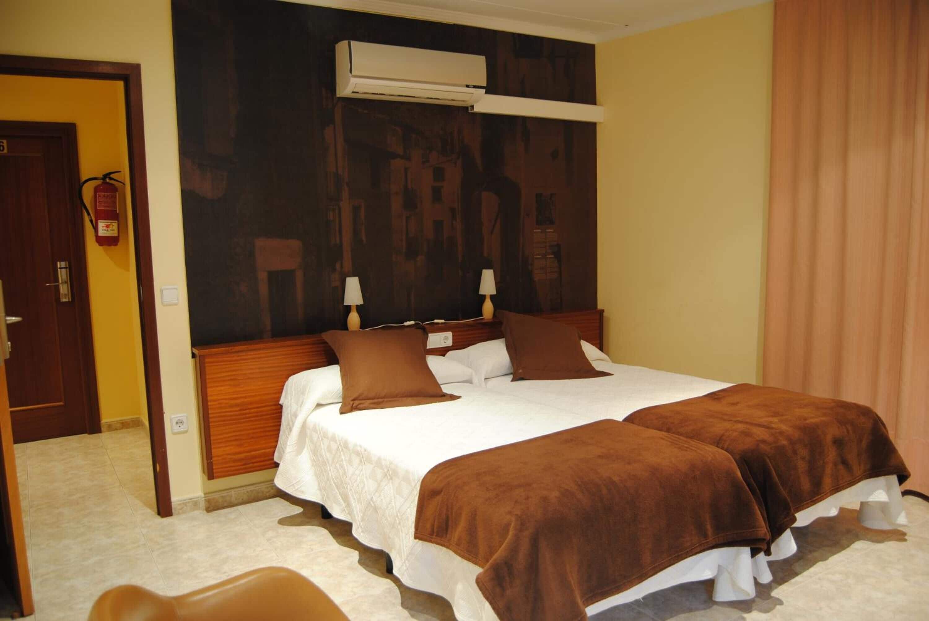 Cama de casal com duas mantas marrons, cabeceira de madeira e ar condicionado fixado na parede.