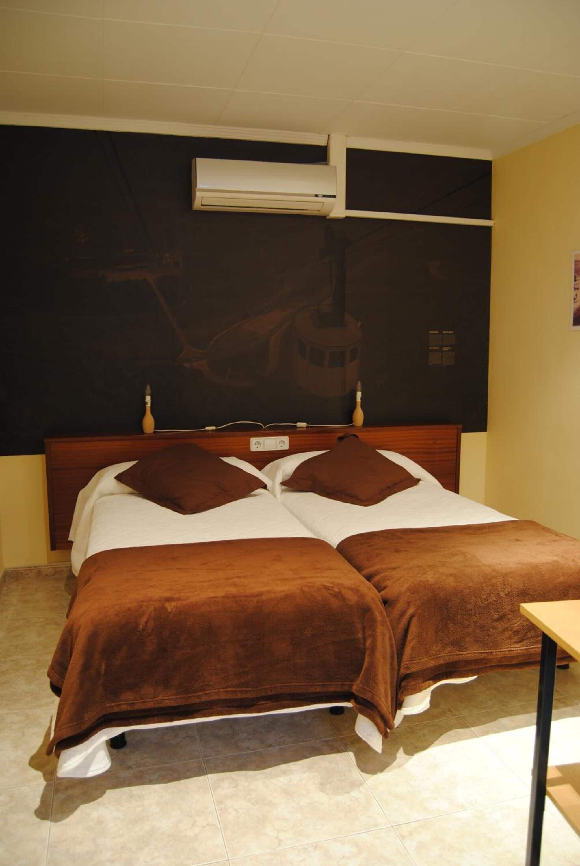 Cama de casal com roupa de cama marrom, cabeceira de madeira e um aparelho de ar condicionado acima.