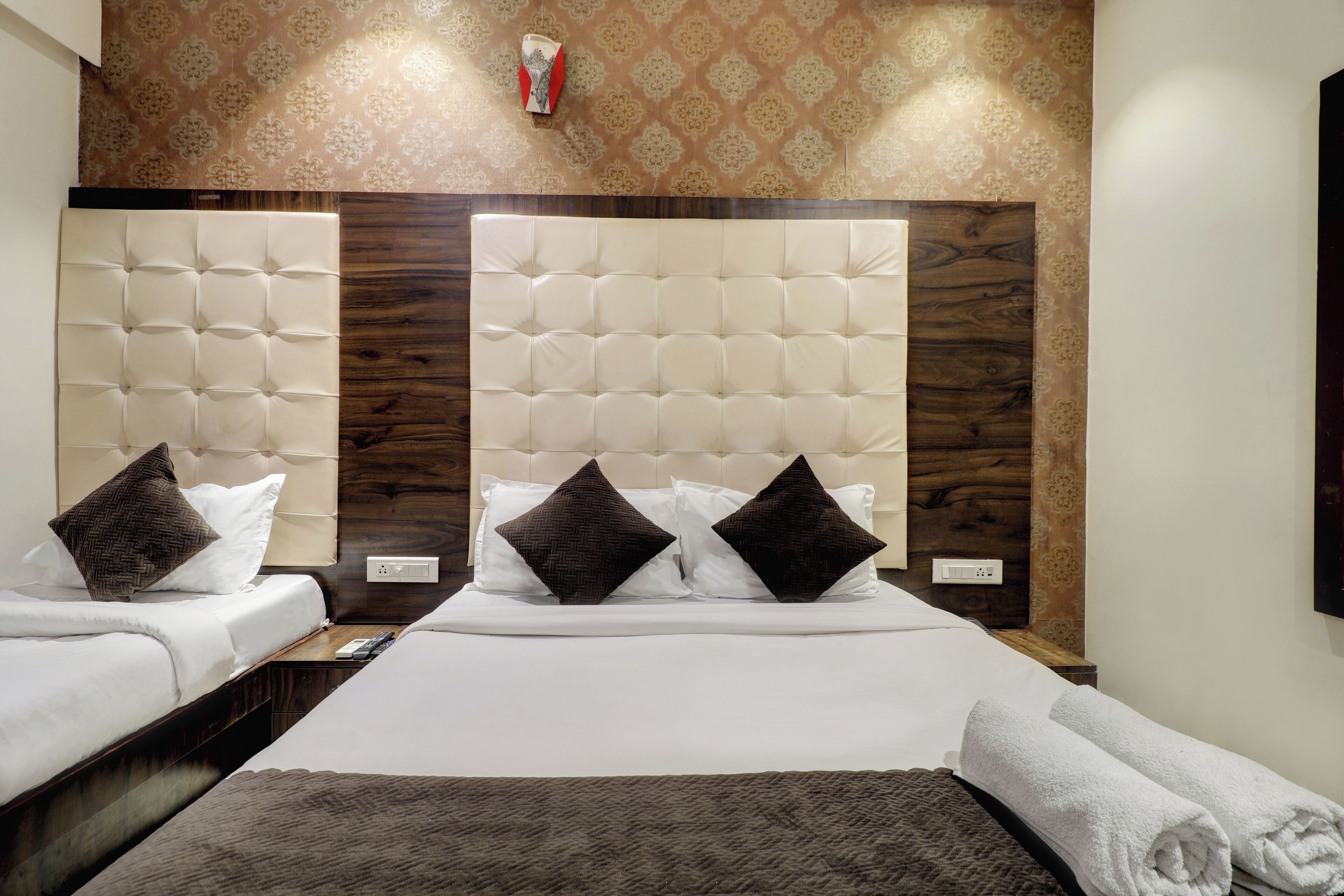 Quarto de hotel com duas camas, cada uma com cabeceira estofada, roupa de cama branca e almofadas castanho escuro.