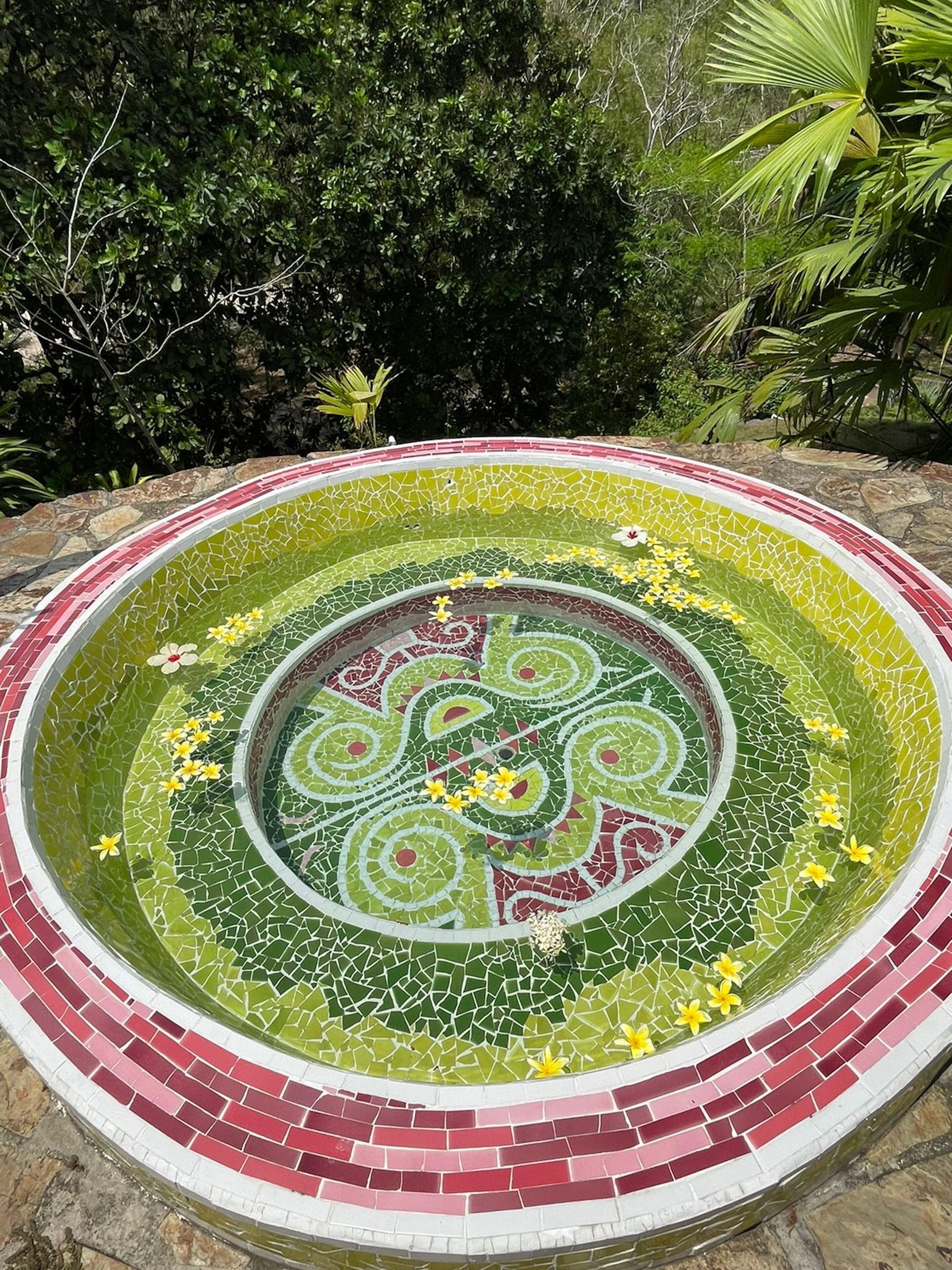 Piscina em mosaico circular com um desenho central, rodeada por uma borda de tijolos vermelhos.