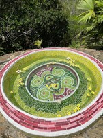 Piscina em mosaico circular com um desenho central, rodeada por uma borda de tijolos vermelhos.