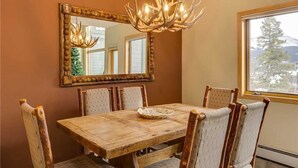 Uma sala de jantar com uma mesa de madeira, seis cadeiras, um espelho grande e um candelabro.