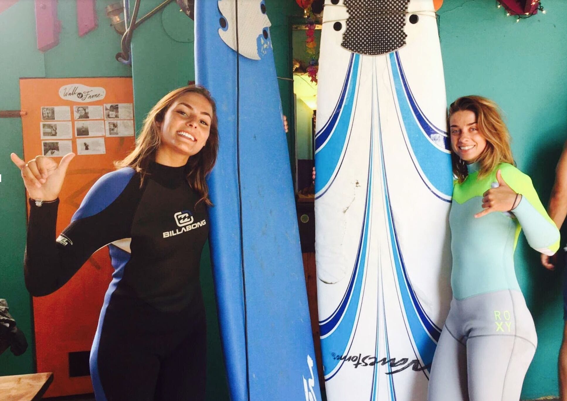 Duas pessoas com fatos de neoprene ao lado de uma prancha de surf.