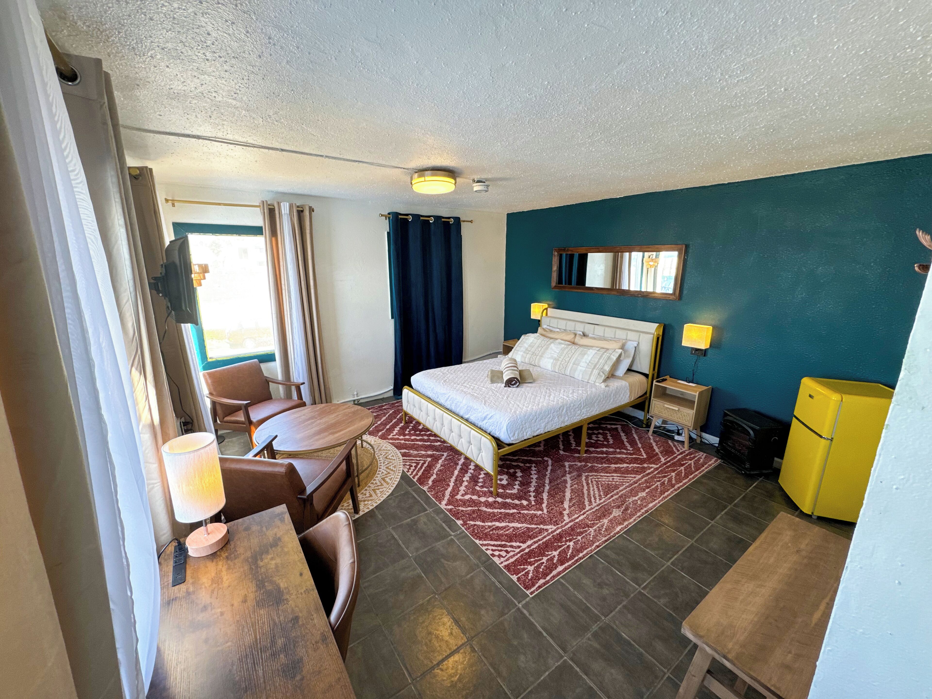 Quarto de hotel com cama, mesas de cabeceira, escrivaninha e uma cadeira.