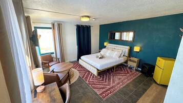 Quarto de hotel com cama, mesas de cabeceira, escrivaninha e uma cadeira.