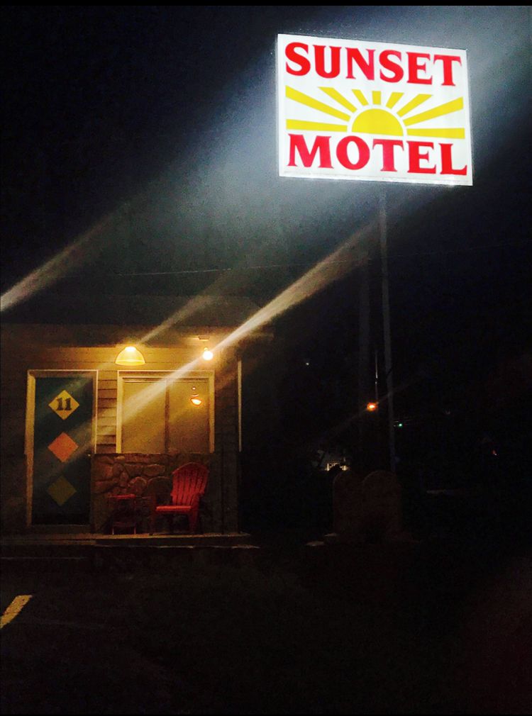 Placa de motel com ilustração de um sol, uma porta com número e uma cadeira do lado de fora.