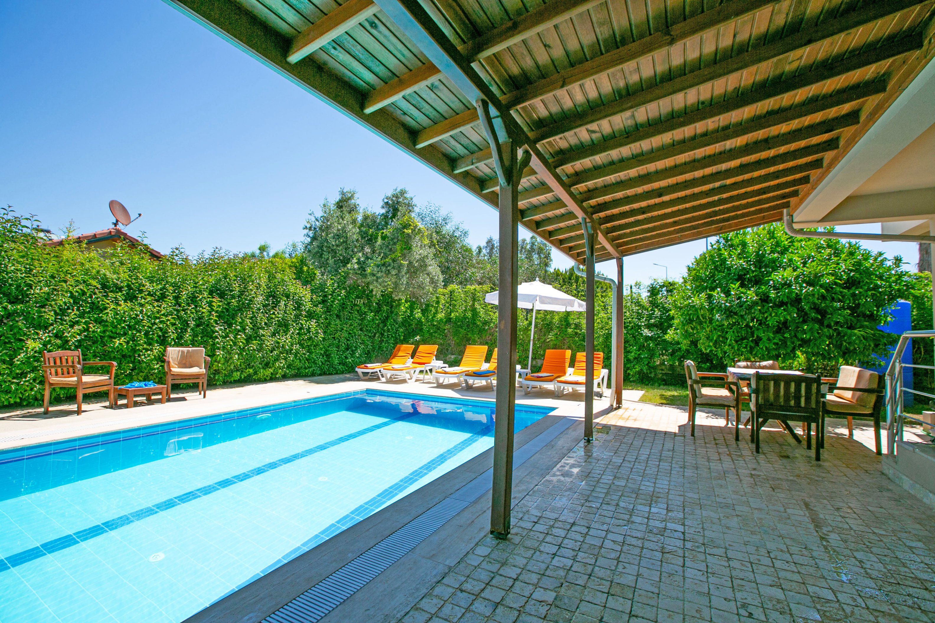 Uma piscina com espreguiçadeiras e um terraço coberto.