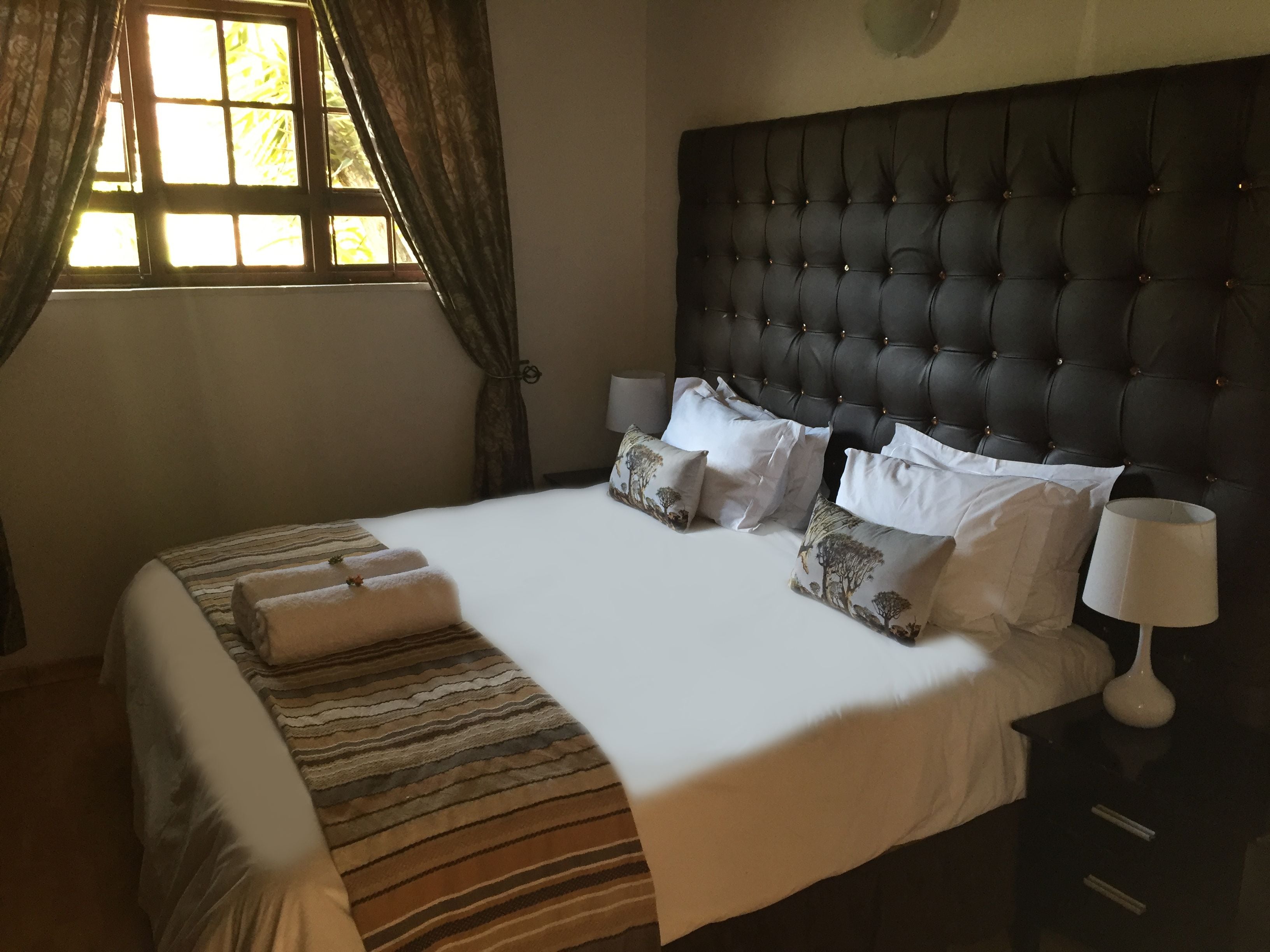 Cama bem arrumada com um cobertor listrado e várias almofadas, uma cabeceira escura com detalhe matelassê e um abajur de cabeceira.