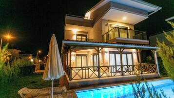 Uma casa de dois andares com piscina, área de estar ao ar livre e varanda coberta.