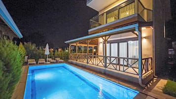 Piscina com área coberta, cercada por vegetação e céu noturno.