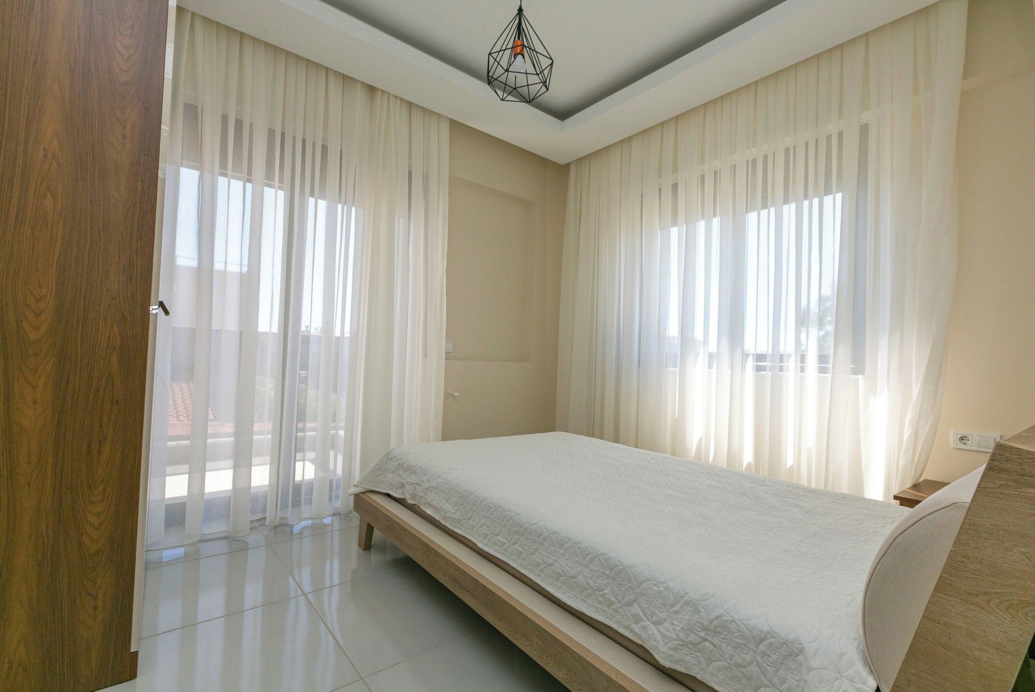Quarto com cama, cortinas e luminária de teto.