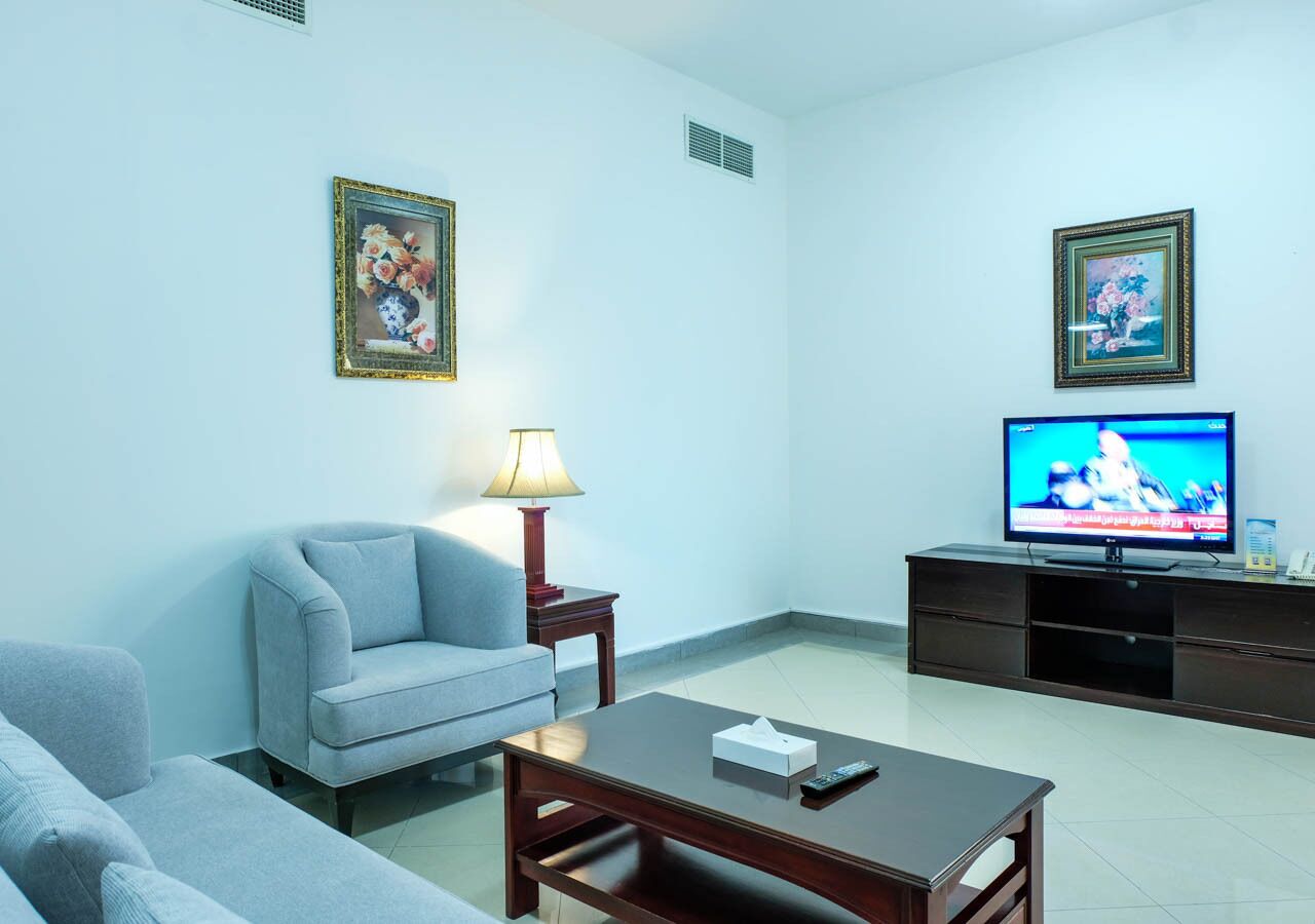 Uma sala de estar com sofá, mesa de centro, televisão e quadros nas paredes.