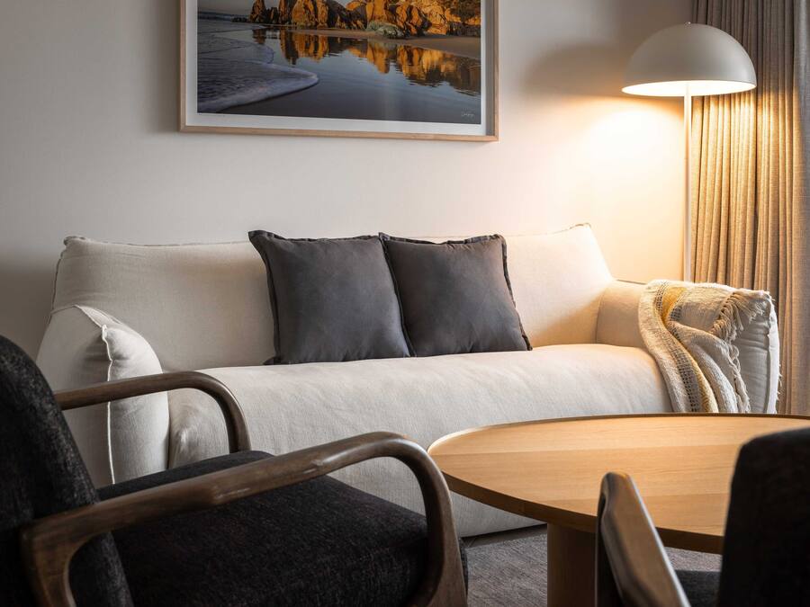 Uma sala de estar moderna com sofá, duas poltronas, mesa de centro de madeira, luminária de chão e um quadro na parede.
