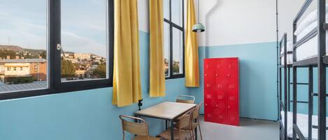 Quarto com mesa e cadeiras, um armário vermelho, beliches e vista pela janela.