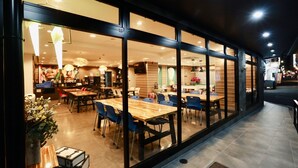 Um restaurante com janelas amplas, mesas de madeira e cadeiras azuis.