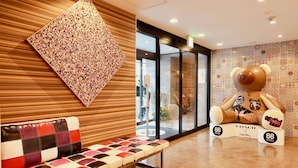 Um hall de hotel com uma obra de arte abstrata e colorida na parede, um banco com almofada xadrez e uma grande estátua de urso de pelúcia com o número 88.
