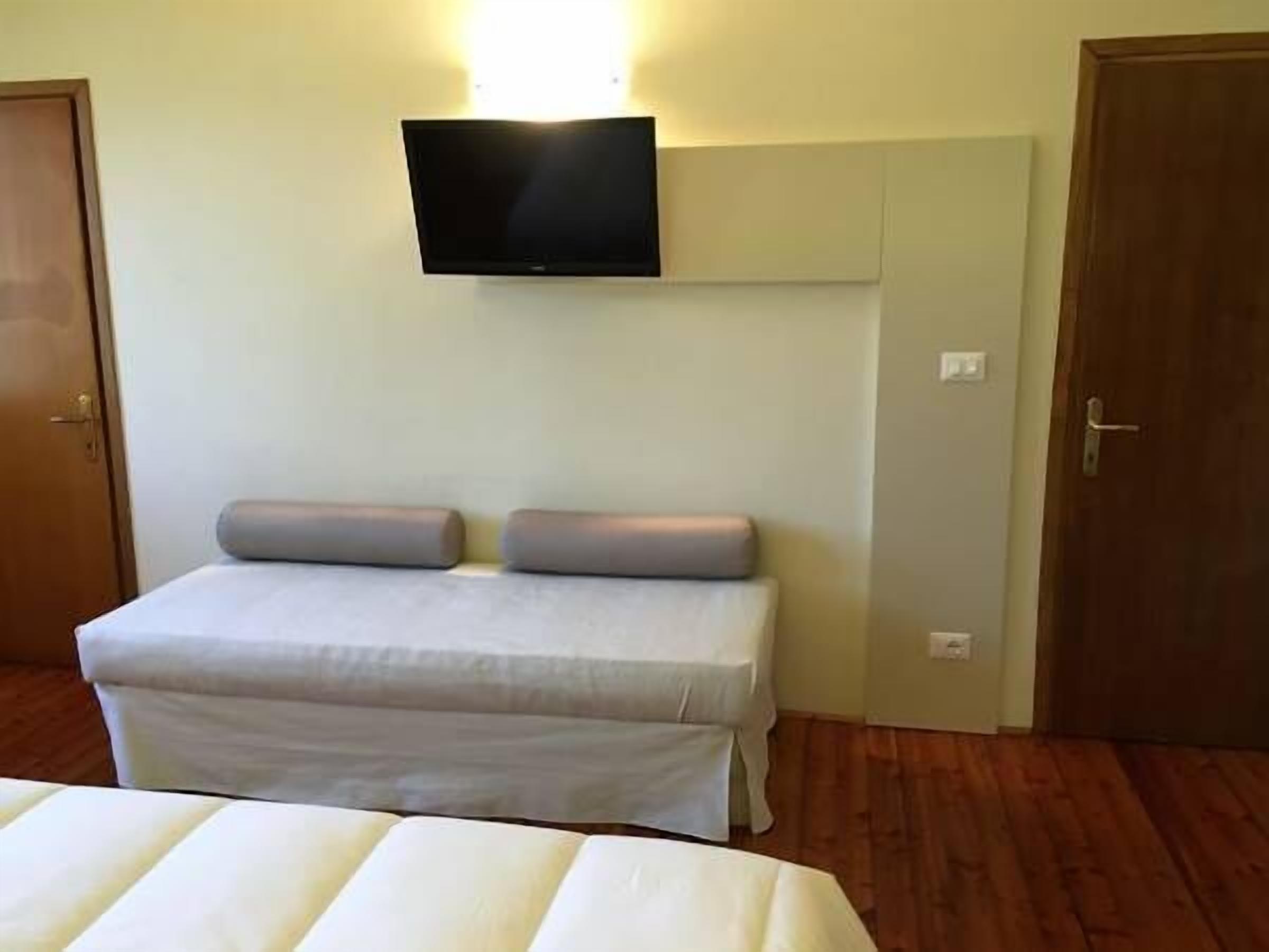 Quarto de hotel com uma cama, televisão fixada na parede e porta de madeira.