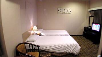 Quarto de hotel com duas camas, uma cadeira, uma televisão e ar condicionado fixado na parede.